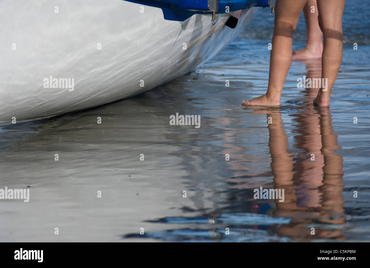 Legs and feet of two women beside a surf rescue rowing boat on wet sand ...