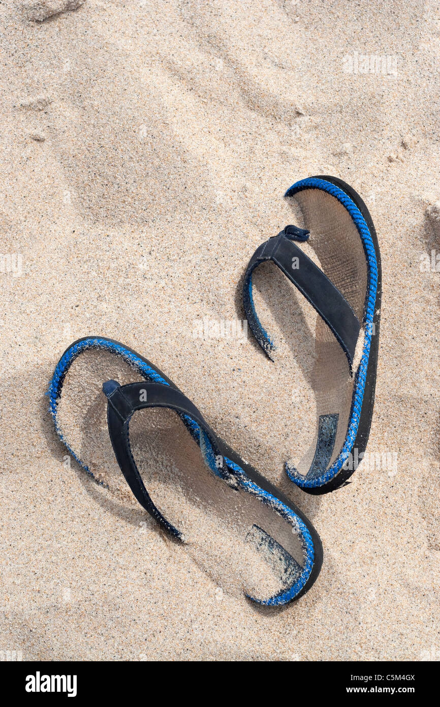 A pair of flip flops or sandals buried in the sand at the beach Stock ...