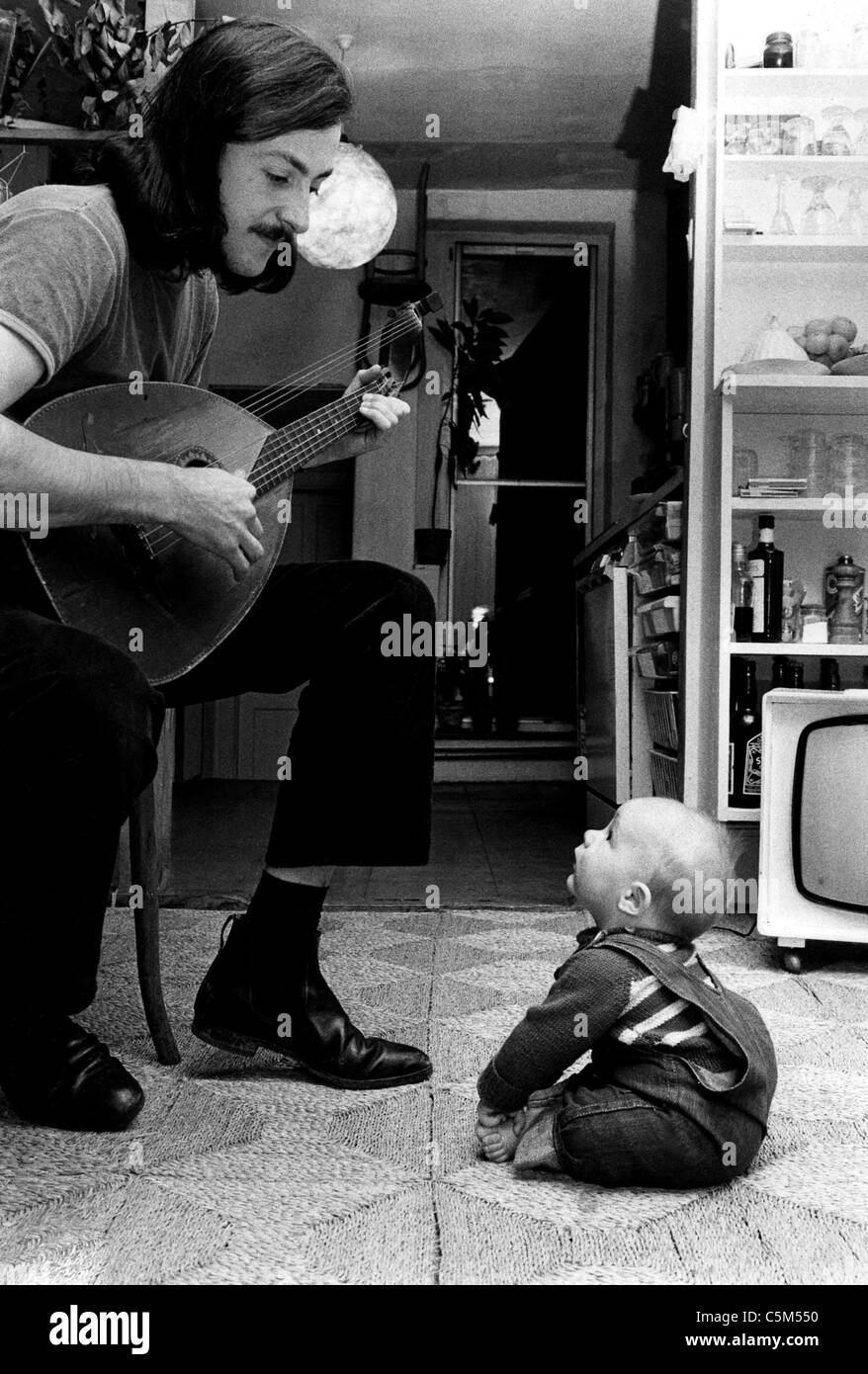 Indoor picture taken in 1969 of father playing a lute with his baby son ...