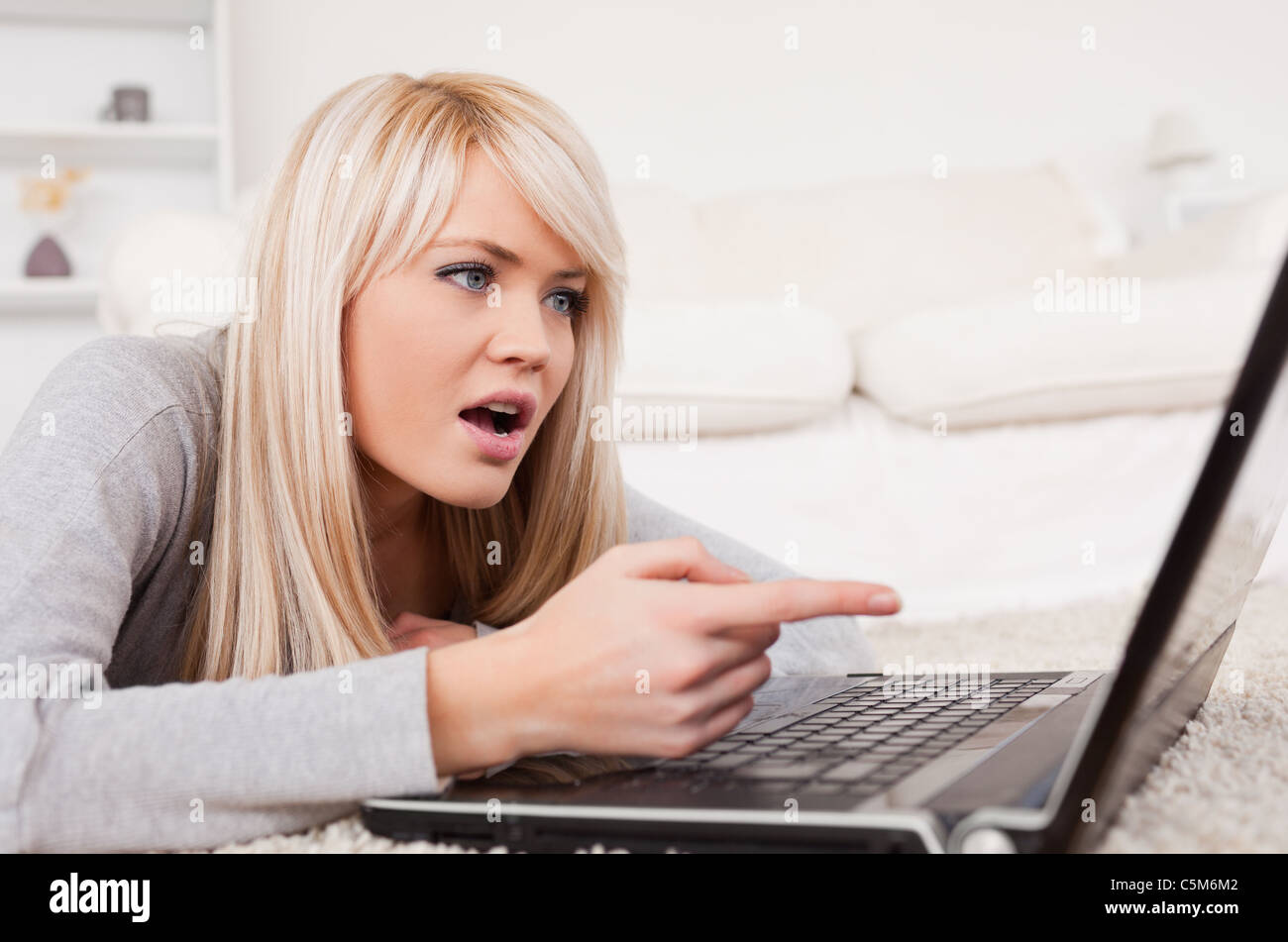 Pretty blond woman frustrated with her computer lying on a carpet Stock ...