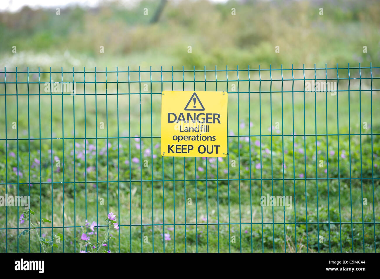 A section of green steel security fence displaying a 'Danger, landfill ...