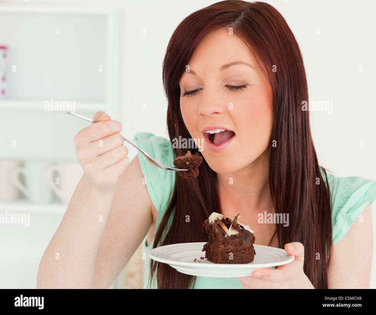 Gorgeous red-haired woman eating some cake in the kitchen Stock Photo ...