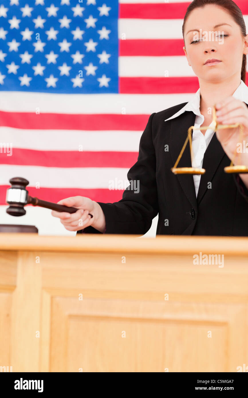 Portrait of a cute judge knocking a gavel and holding scales of justice ...