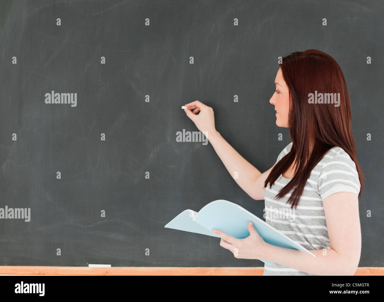 Young woman writting on a blackboard holding her notes Stock Photo - Alamy