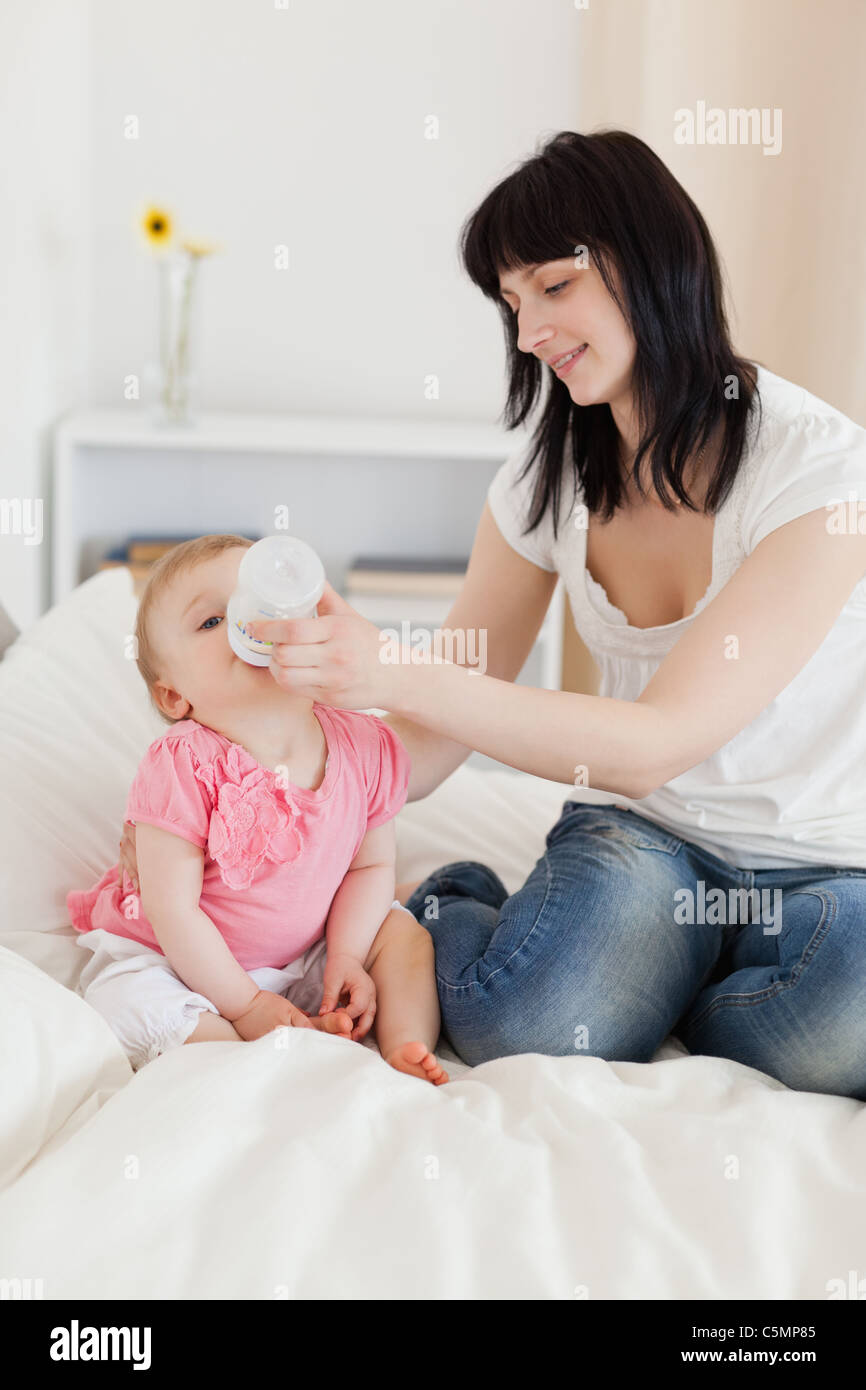 Pretty brunette female bottle-feeding her baby on a bed Stock Photo - Alamy