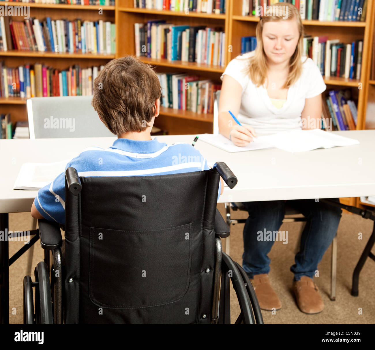 Disabled student in the school library, studying with a classmate ...