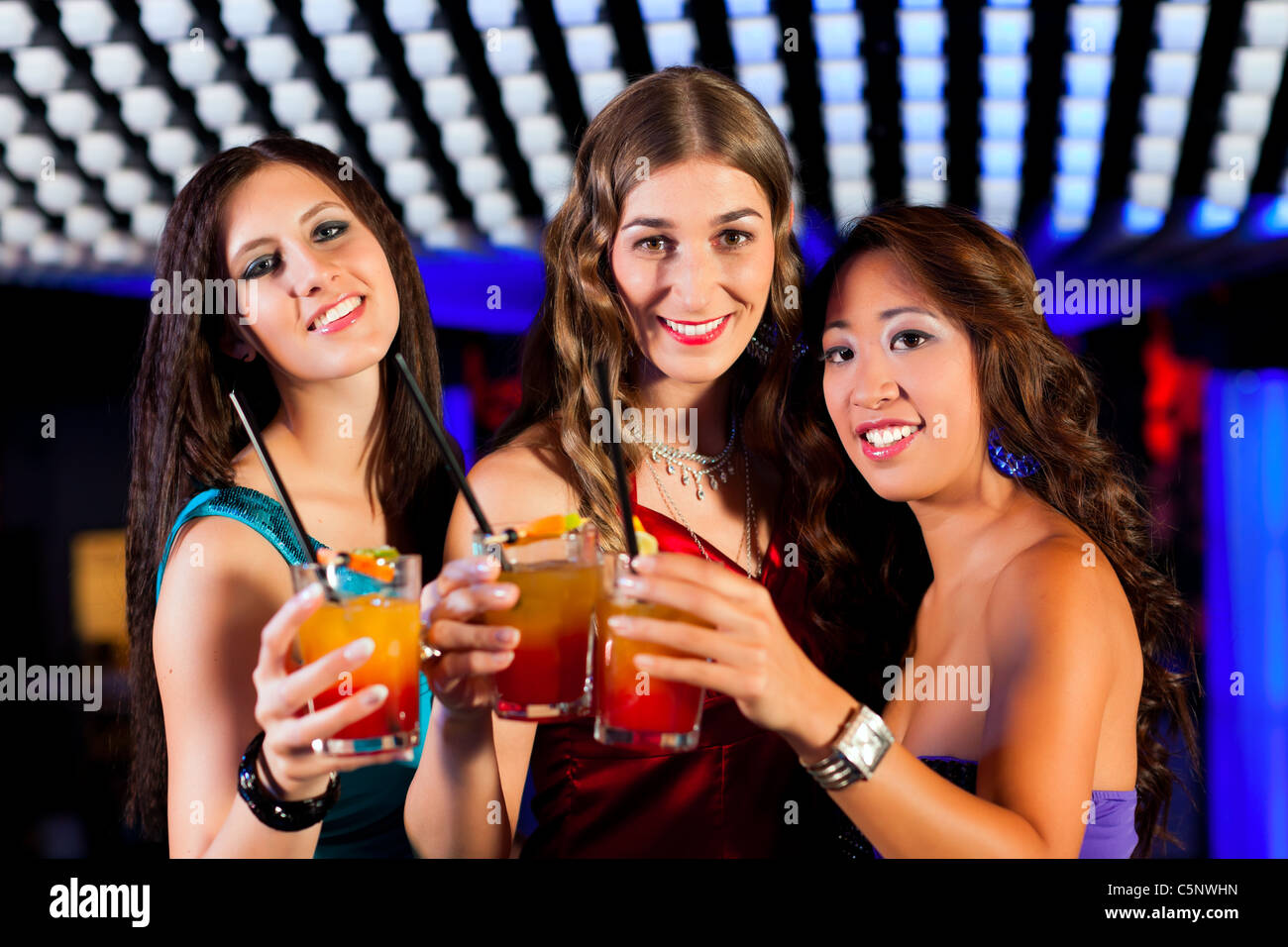 Group of party people - three friends - with cocktails in a bar or club ...