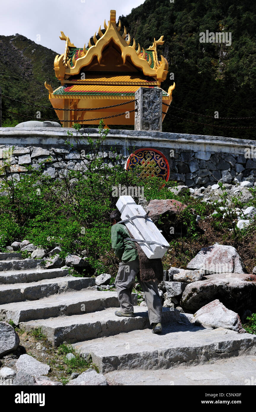 A man carries on his back a stone post to construction site of a ...