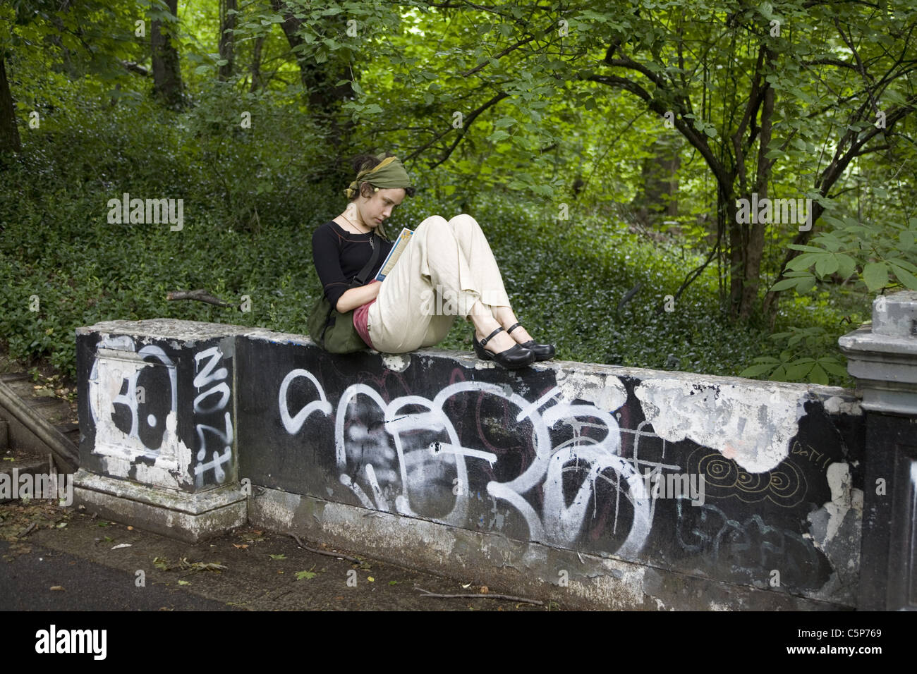 Young woman relaxes with a book on a decaying, graffiti marked stairway ...