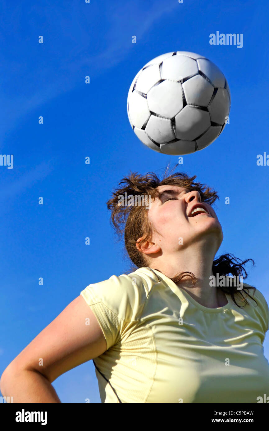 Young woman teenager heading the football or soccer ball during a match ...