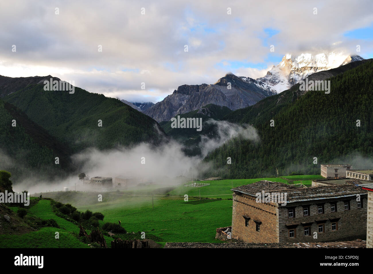 Morning fog covers Yading village. Xiannairi in the background ...