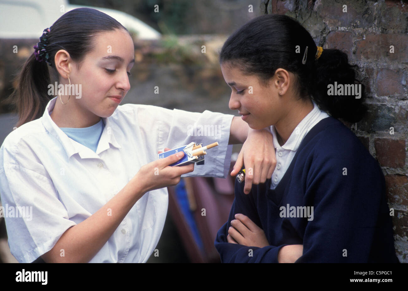 two secondary schoolgirls smoking behind wall Stock Photo - Alamy
