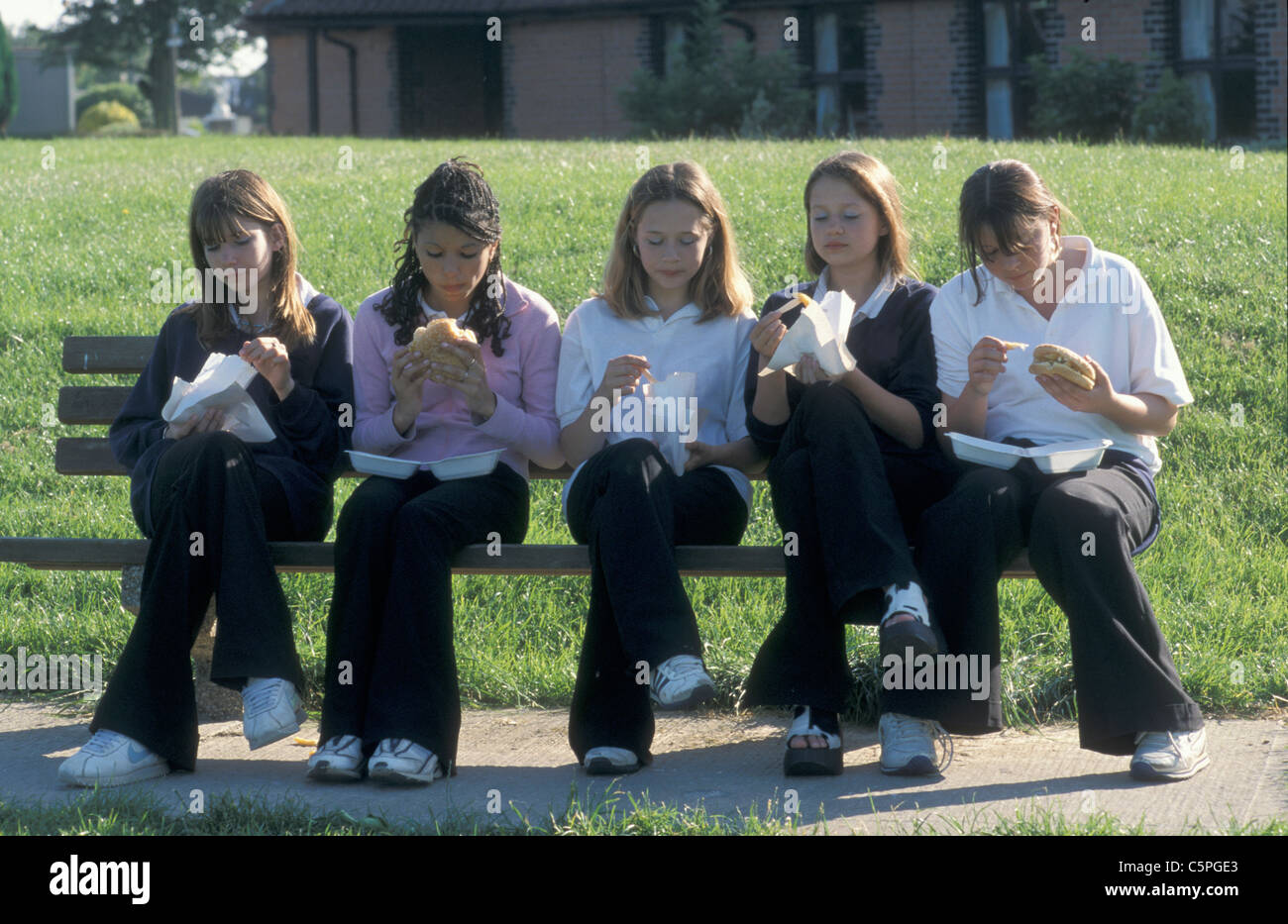 Five girls sitting on bench at school lunch-break time eating burger ...