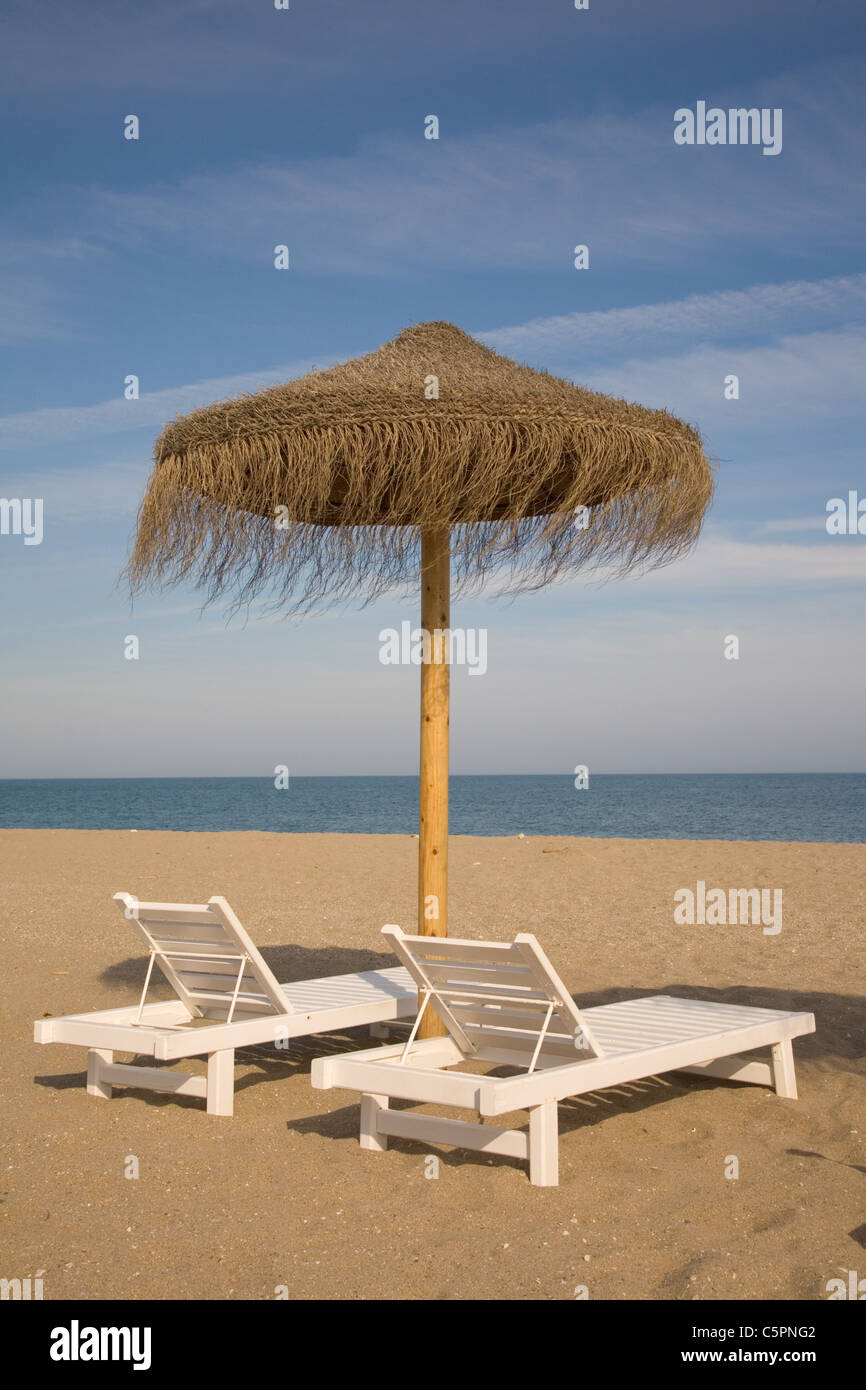 Beach loungers on a quiet Spanish beach with grass parasol against a ...