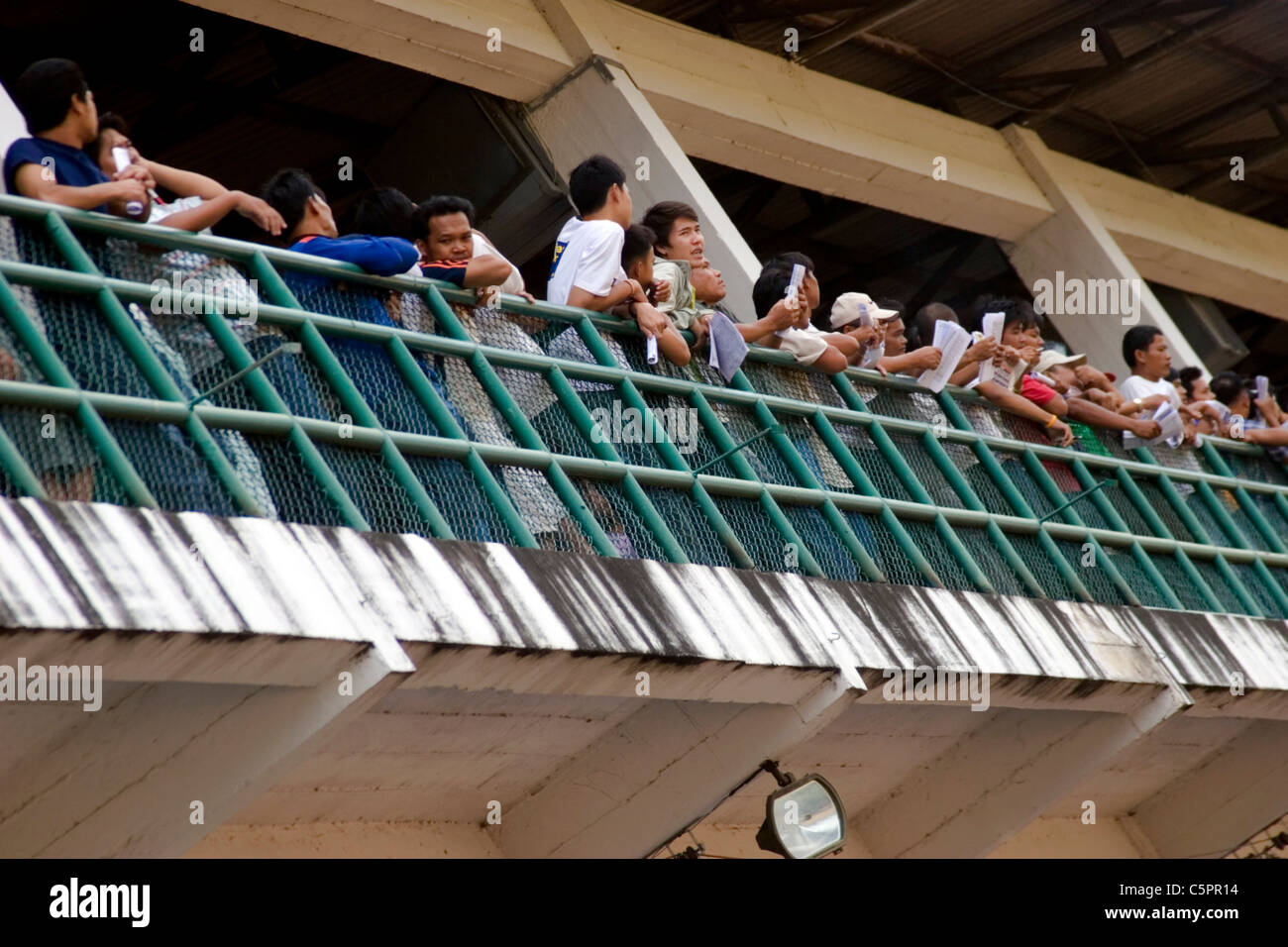 Horse racing fans are leaning on a balcony rail watching a horse race ...