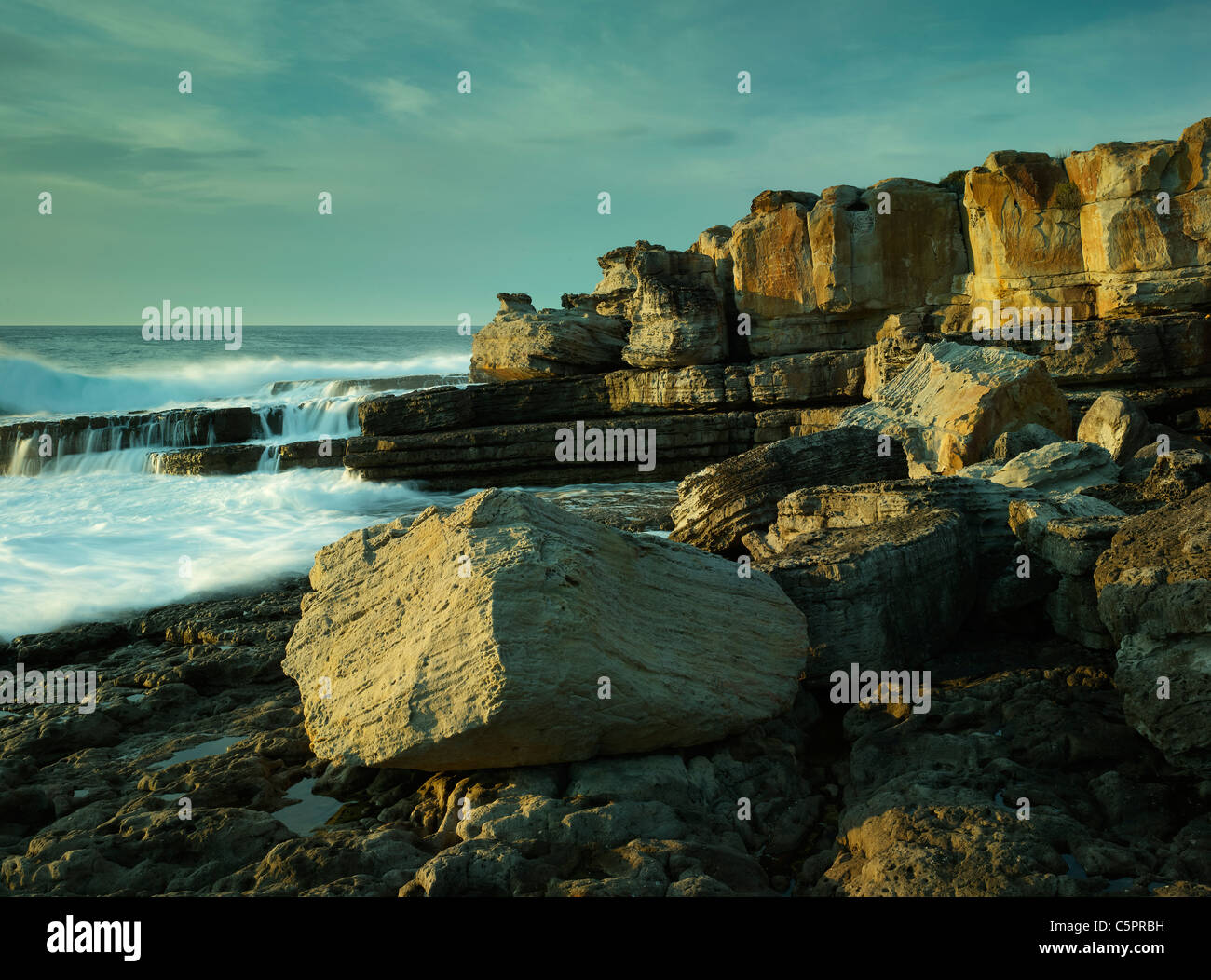 A wave washes over the sloping eroded rock platform amidst a jumble of ...