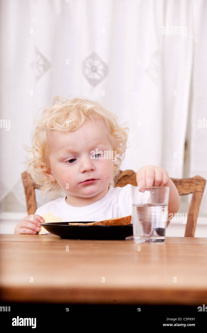 A young child sitting a a table reaching for glass of water Stock Photo ...