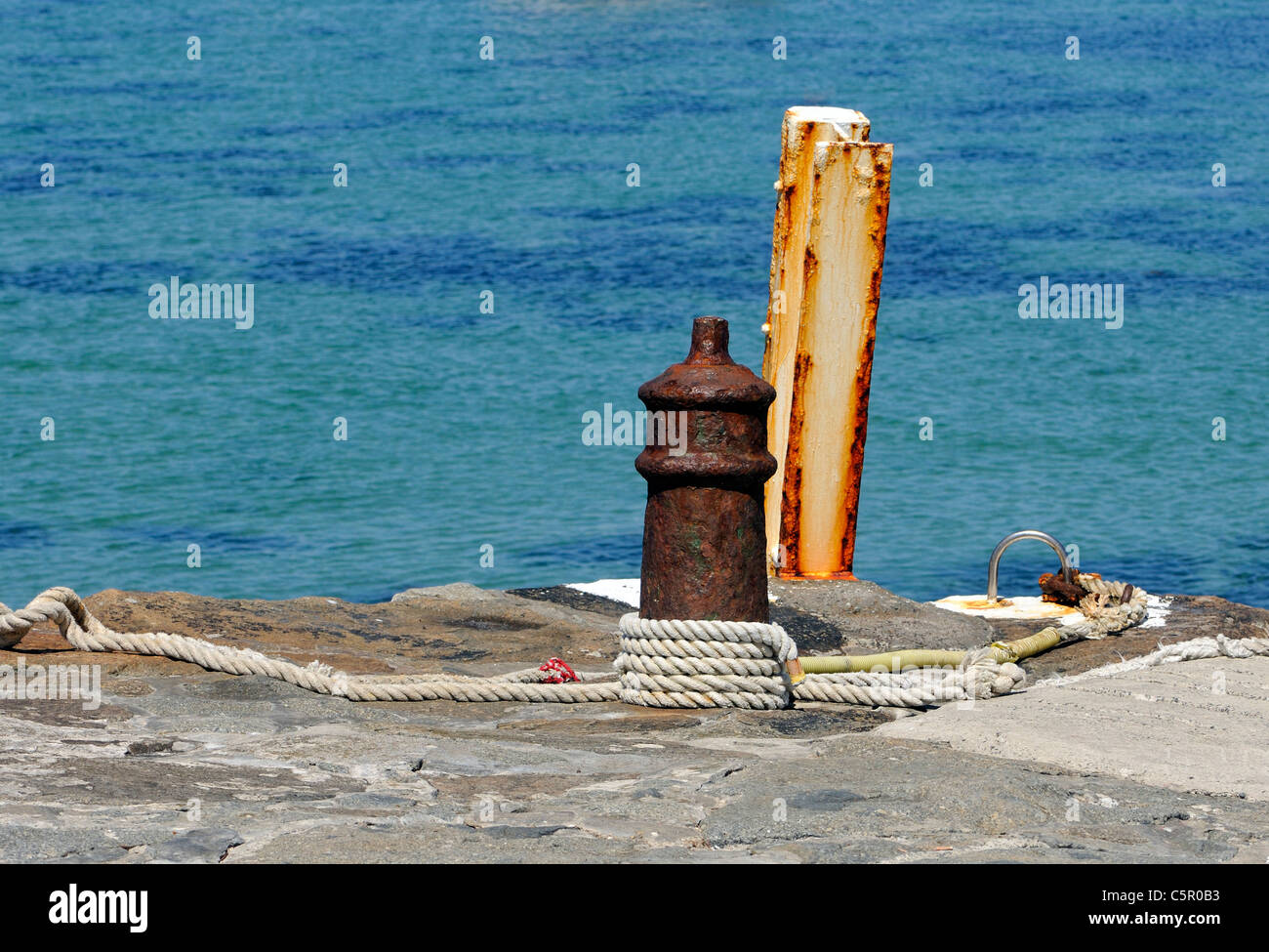 A rope coiled round a rusty iron bollard on the quay of Herm harbour ...