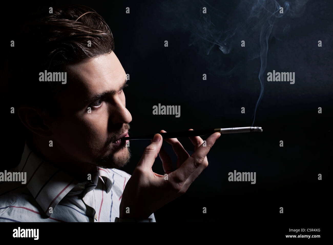 Studio portrait of a young man smoking a cigarette on a black ...