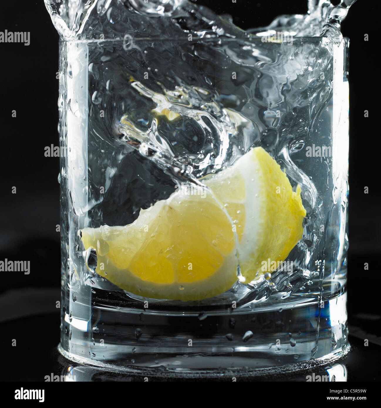 Lemon dropped into glass of water Stock Photo - Alamy
