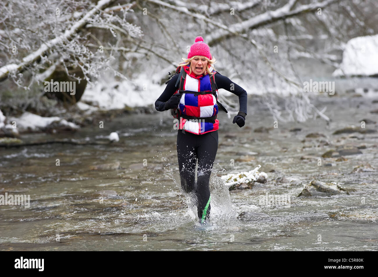 A jogger running through a snowy river bed and it's cold alpine waters ...