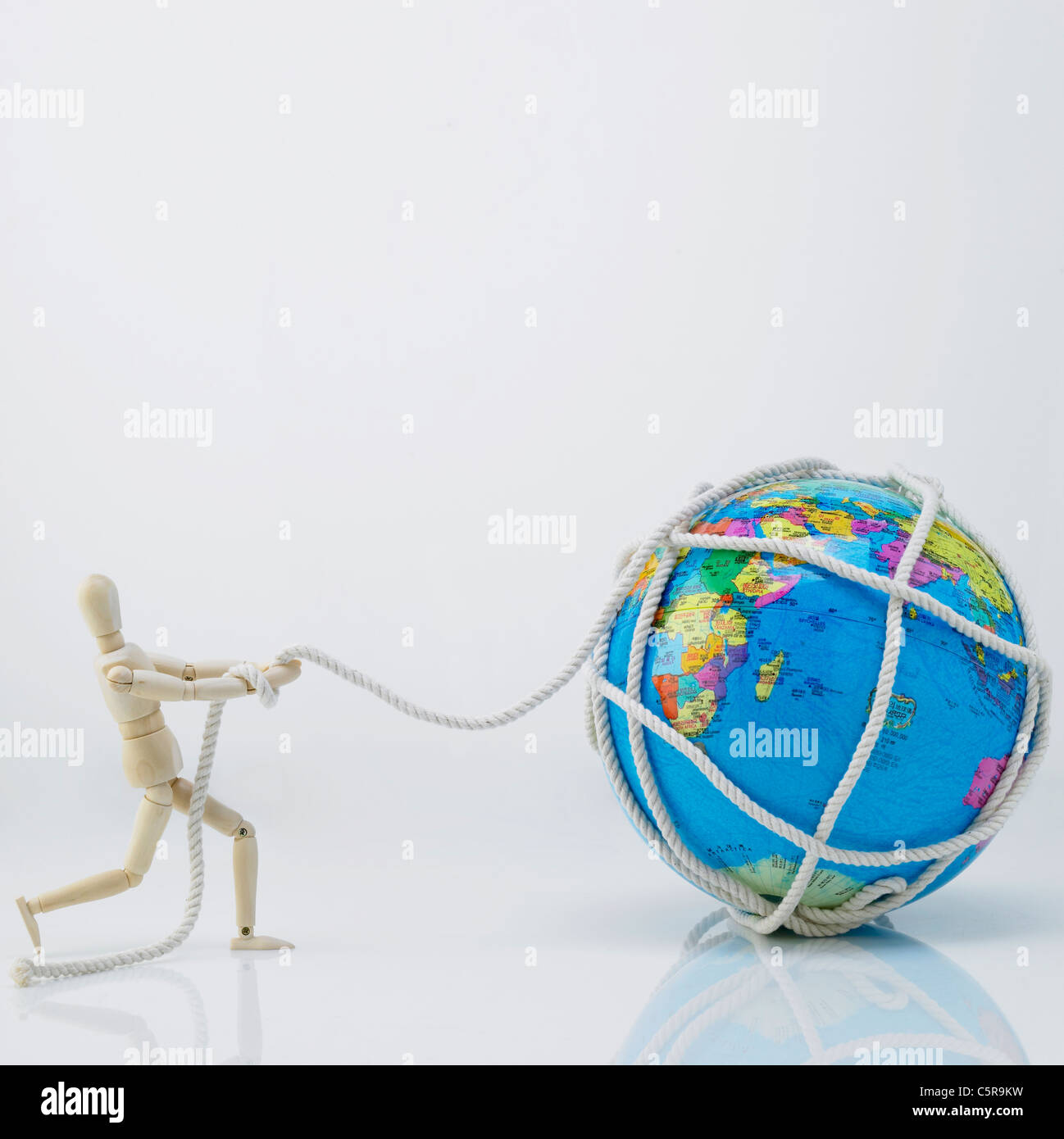 A wooden figurine pulling a globe rolled up by rope Stock Photo - Alamy