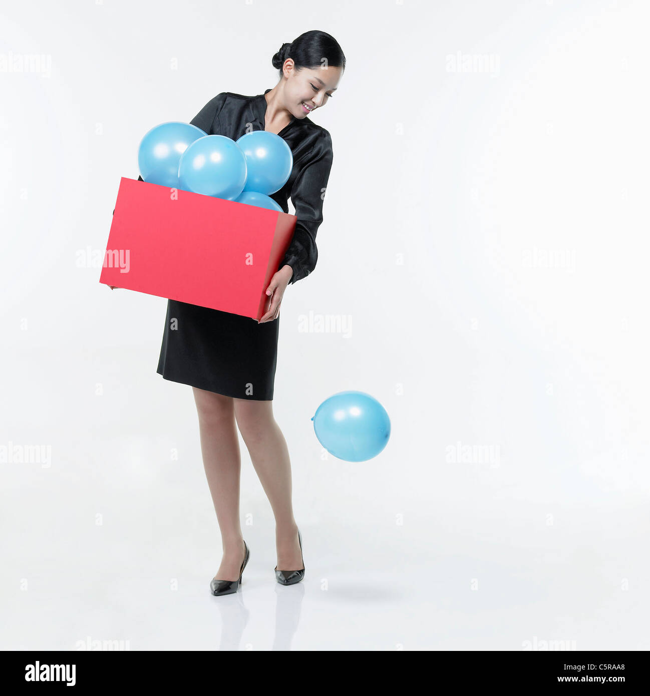 A woman holding a box of balloons and one balloon falling out from the ...