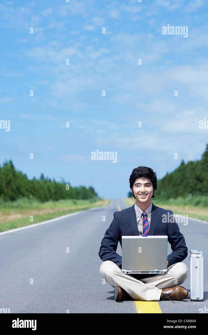 A man sitting on a road doing notebook computer Stock Photo - Alamy
