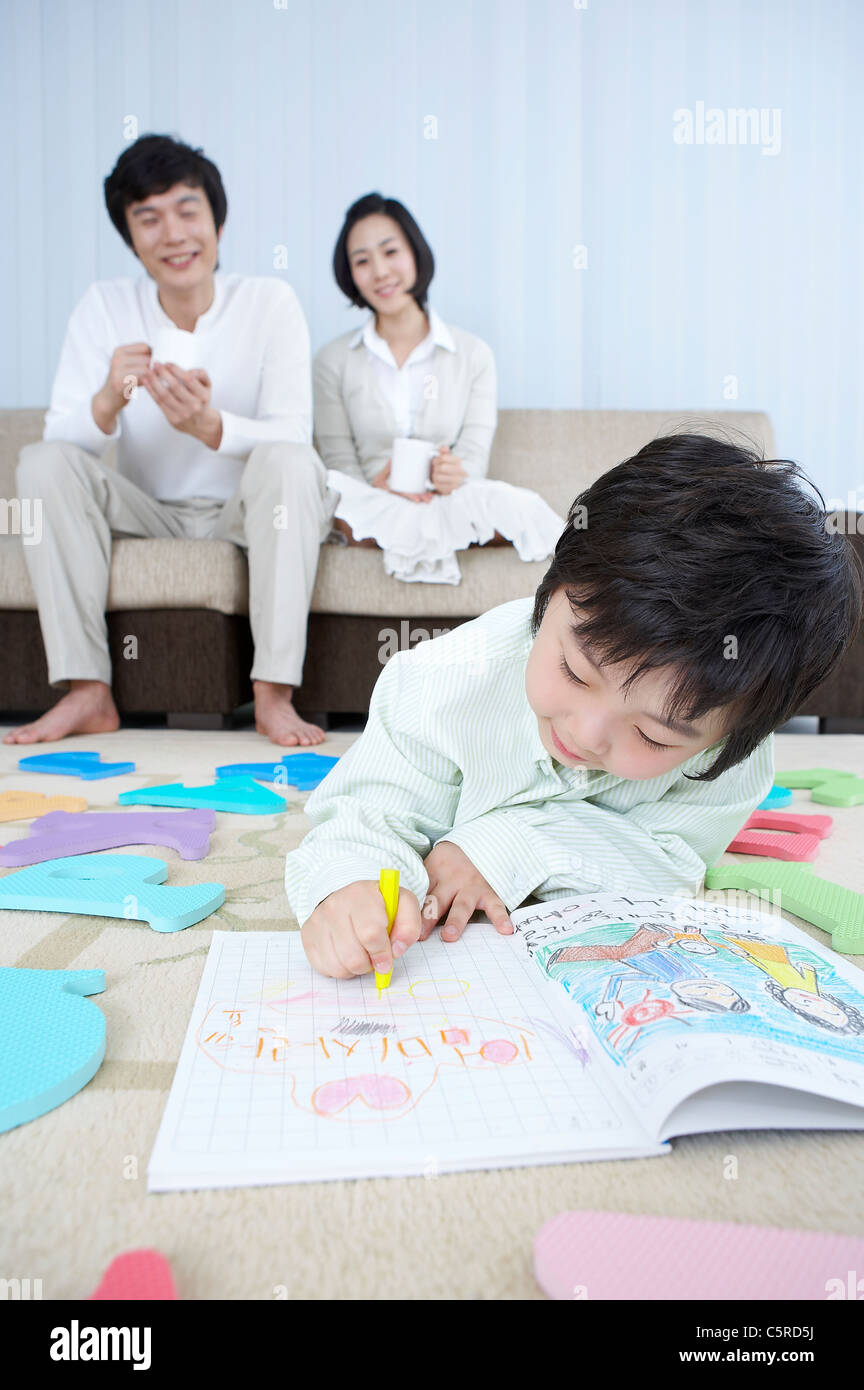 A boy writing in the notebook and his parents looking at him Stock ...