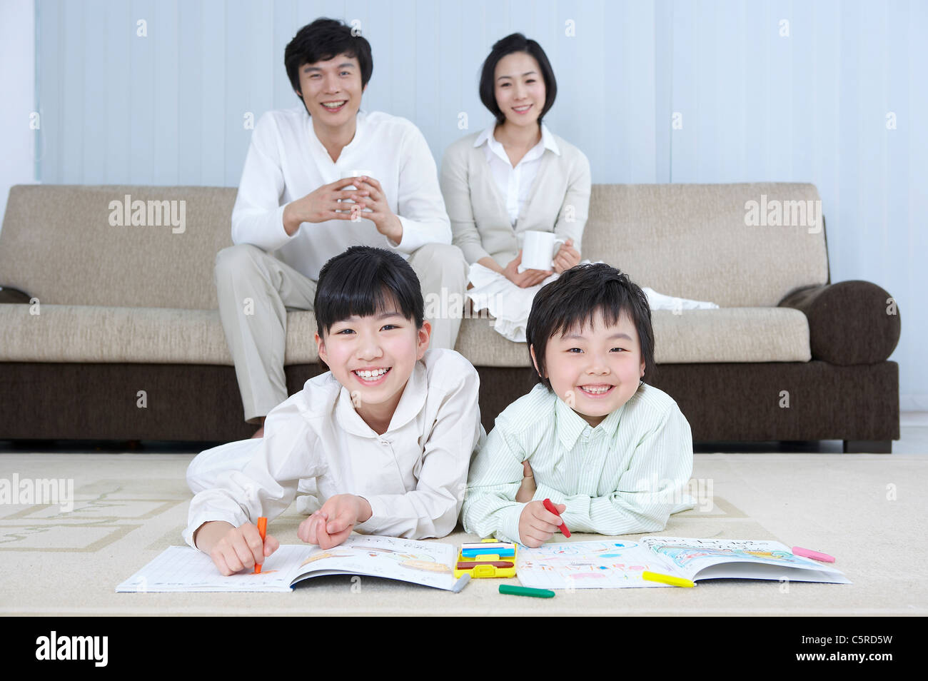 A boy and a girl writing on their notebooks and their parents smiling ...