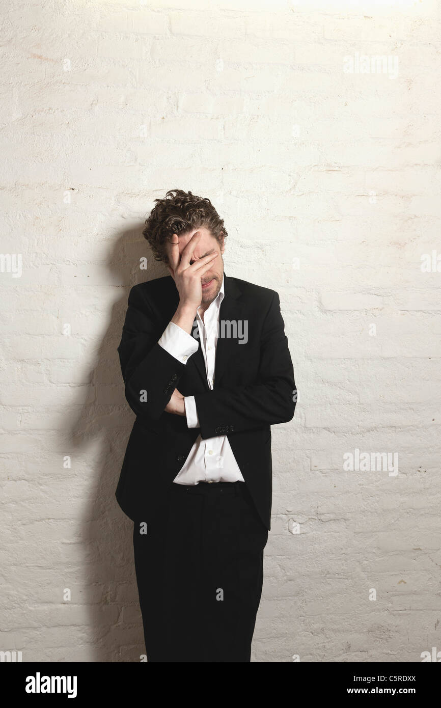 Depressed mid adult man standing against wall Stock Photo - Alamy