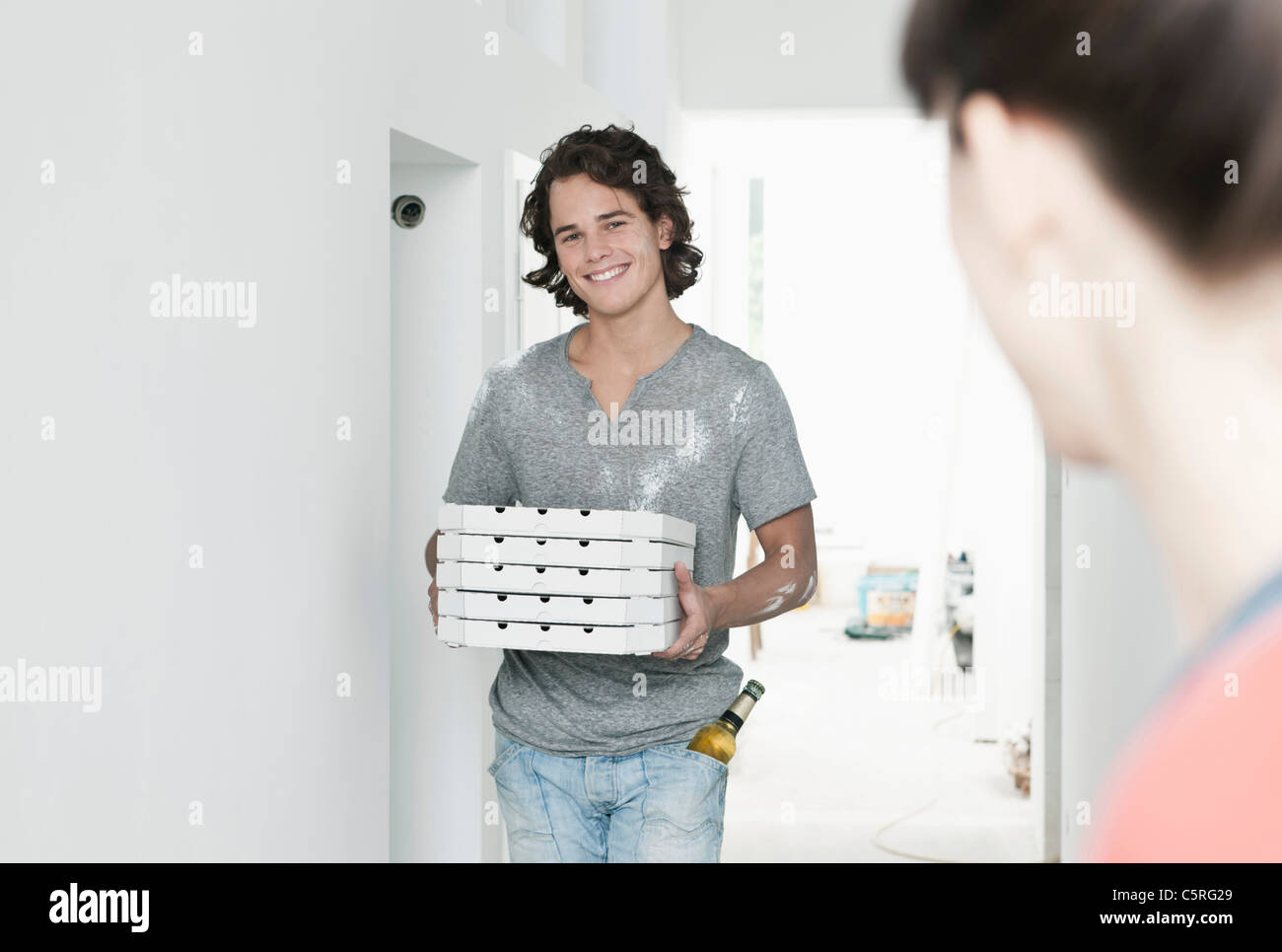 Germany, Cologne, Young man carrying pizza box in renovating apartment ...