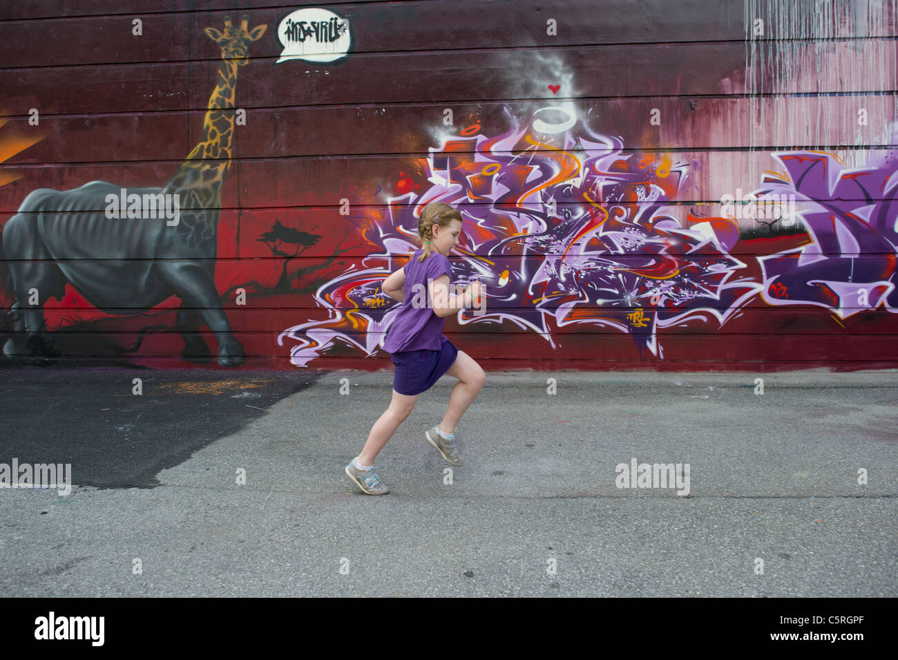 A young girl wearing purple running past a building's wall covered in ...