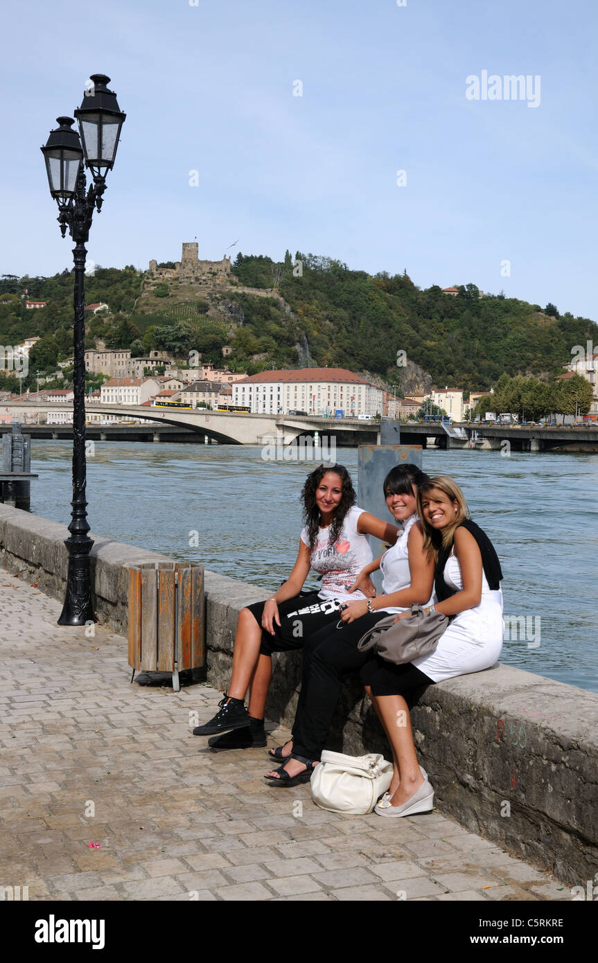 Three young women girls sitting on wall on west bank of river Rhone ...