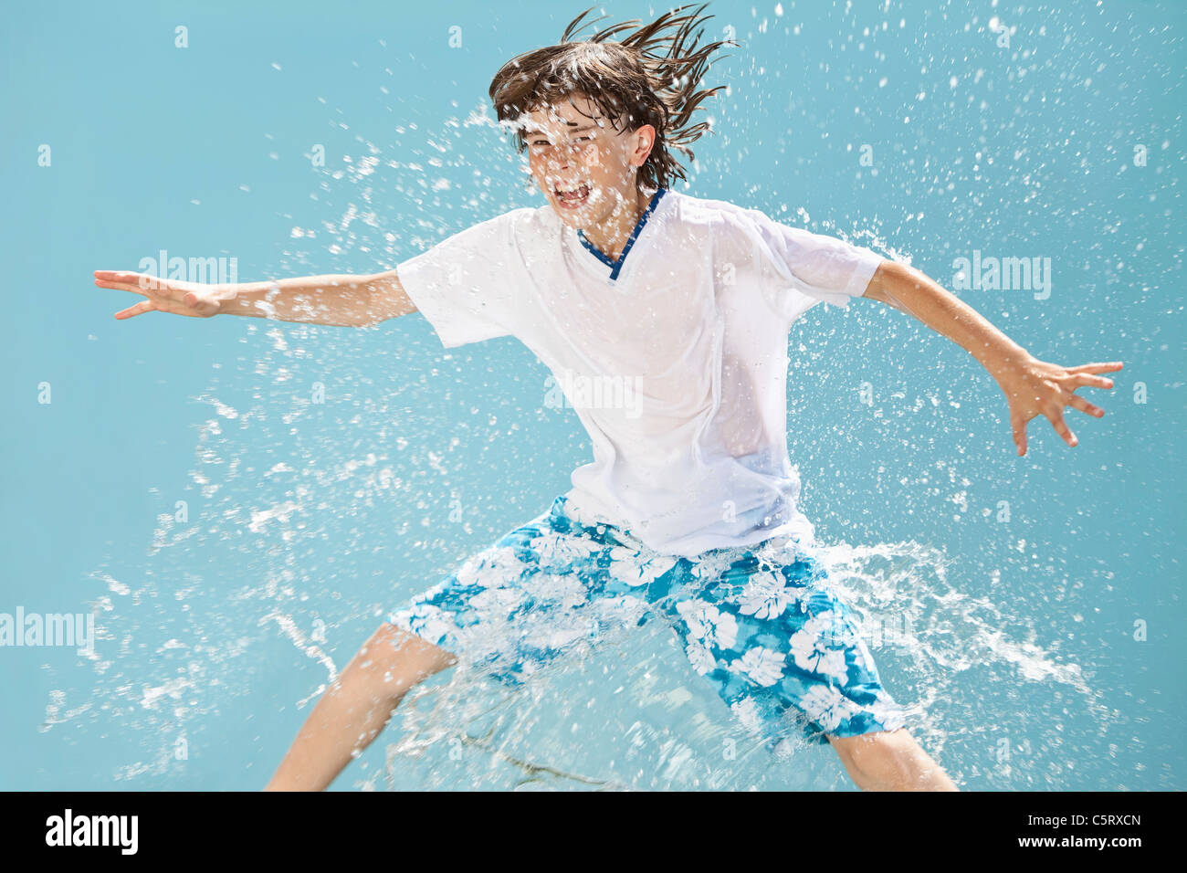 Germany, Boy jumping in splash of water against blue background Stock ...