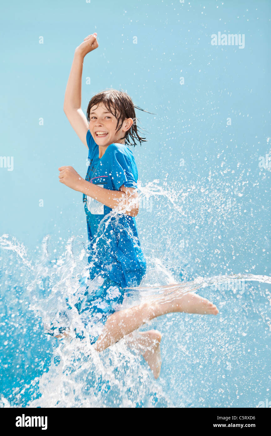 Germany, Boy jumping in splash of water against blue background Stock ...