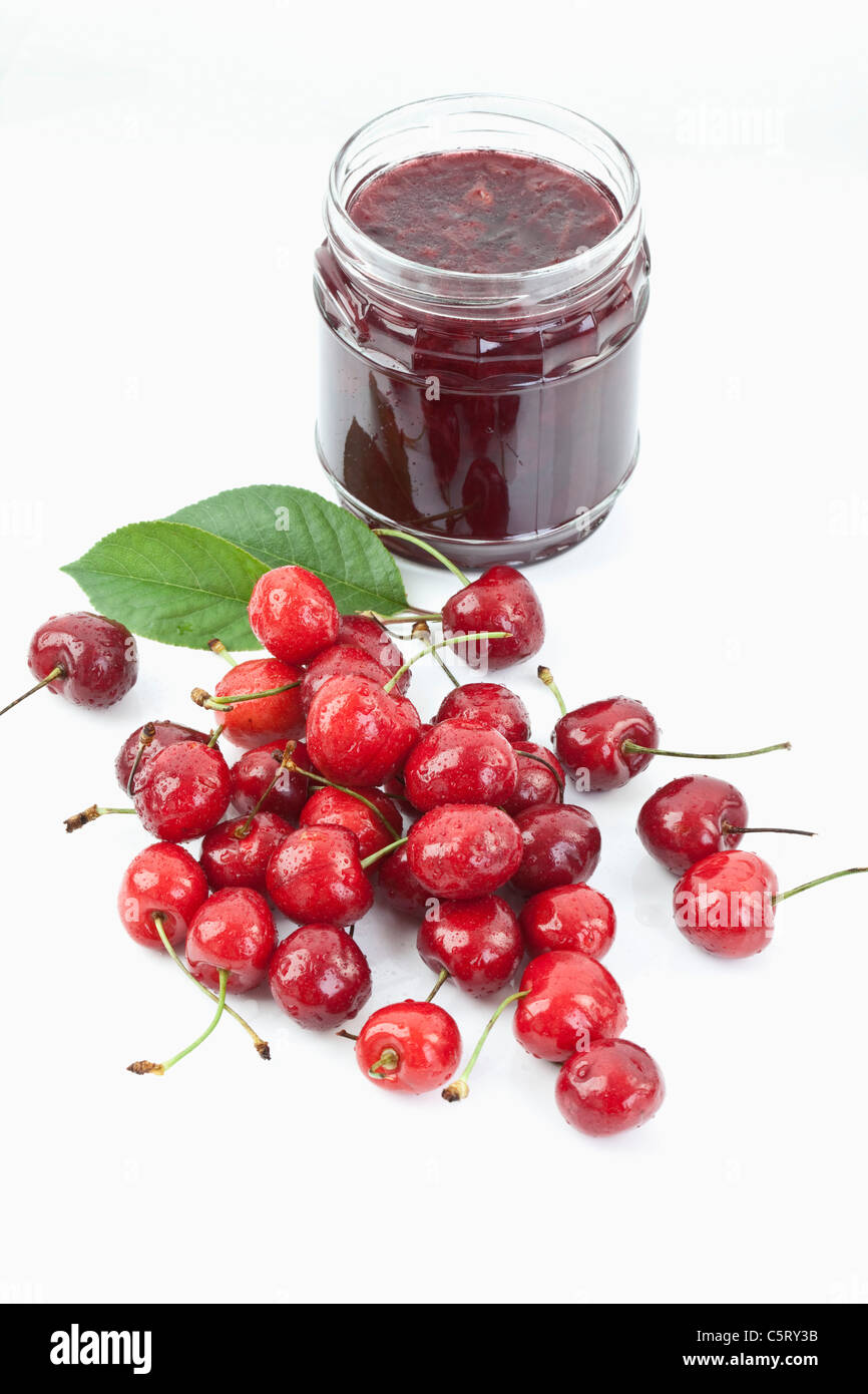 Cherries beside open jar of cherry jam on white background, close up ...