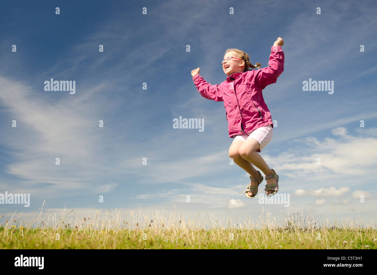 Happy little girl jumping in front of blue sky Stock Photo - Alamy