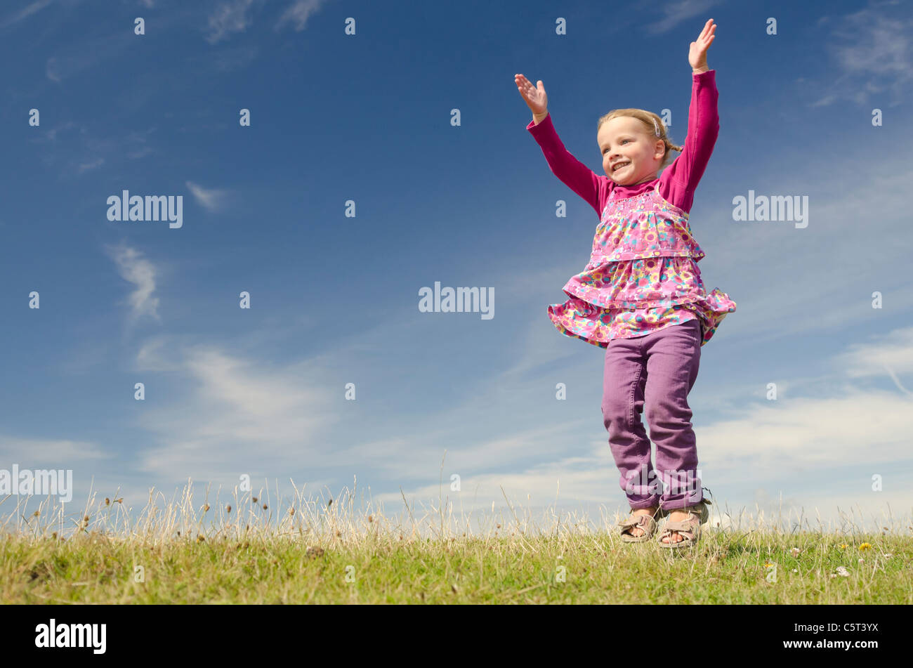 Happy little girl jumping in front of blue sky Stock Photo - Alamy