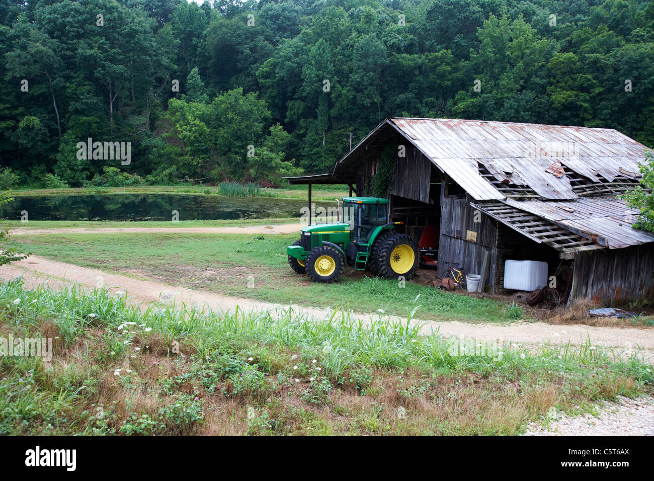 tractor in old worn battered traditional farm building in clearing in ...
