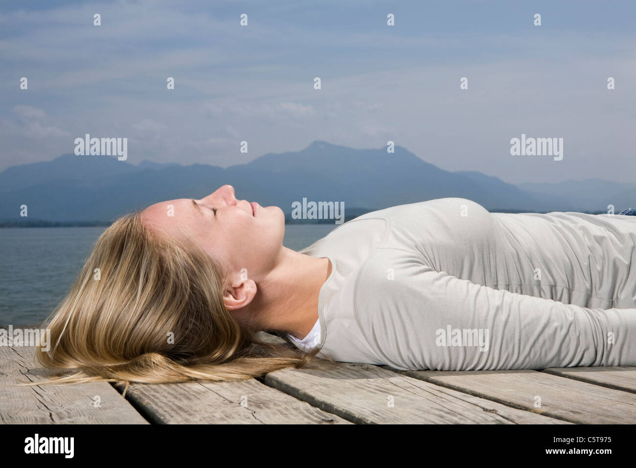 Germany, Chiemsee, Woman lying on jetty, eyes closed, side view ...