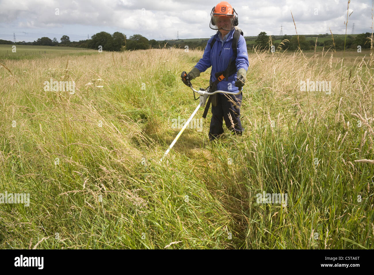 UK Elderly female volunteer dressed in safety equipment using a petrol ...
