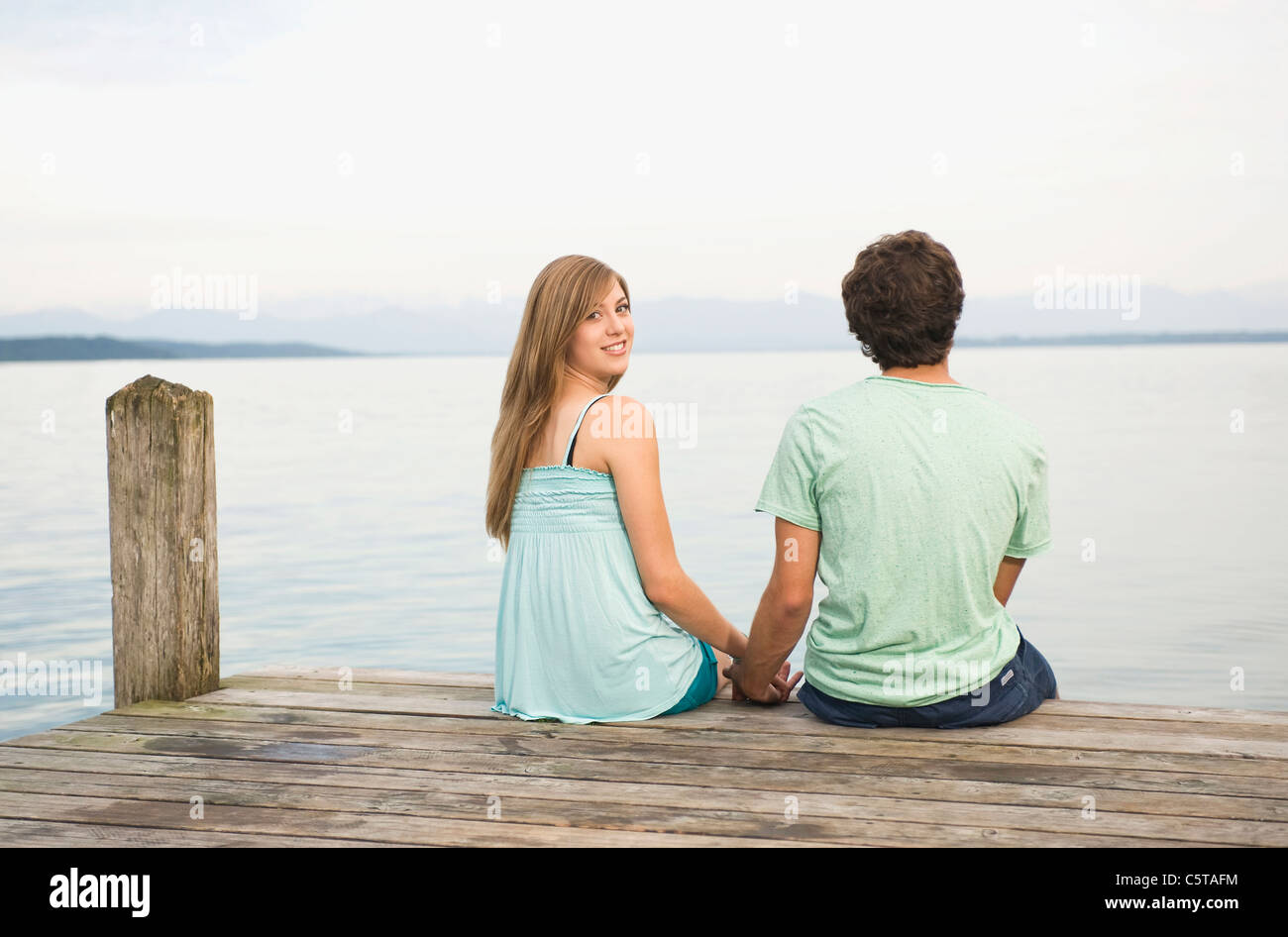 Germany, Bavaria, Starnberger See, Young couple sitting on jetty, rear view Stock Photo - Alamy