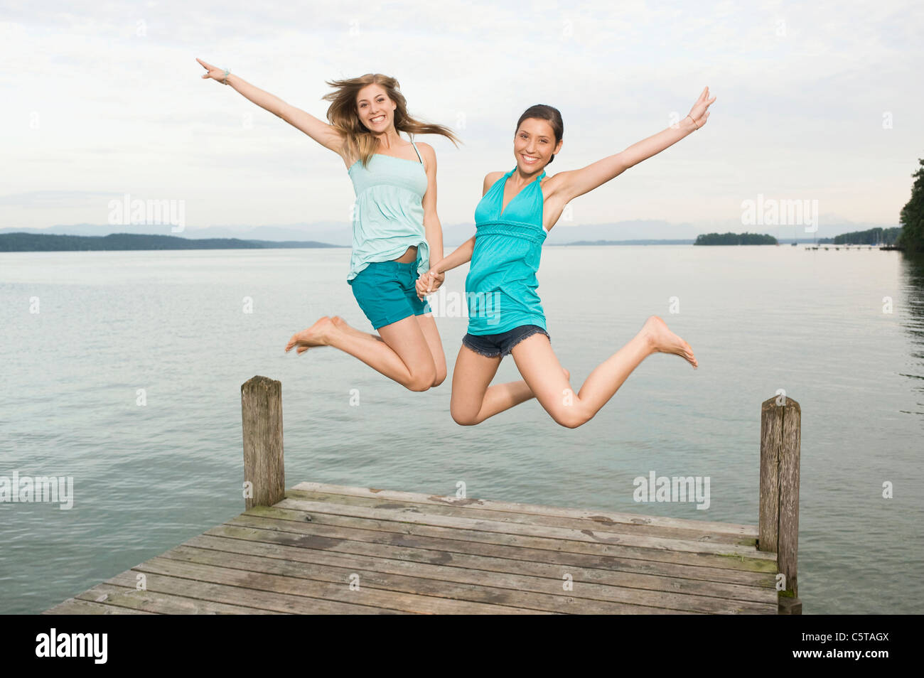 Germany, Bavaria, Starnberger See, Two young women jumping on jetty ...