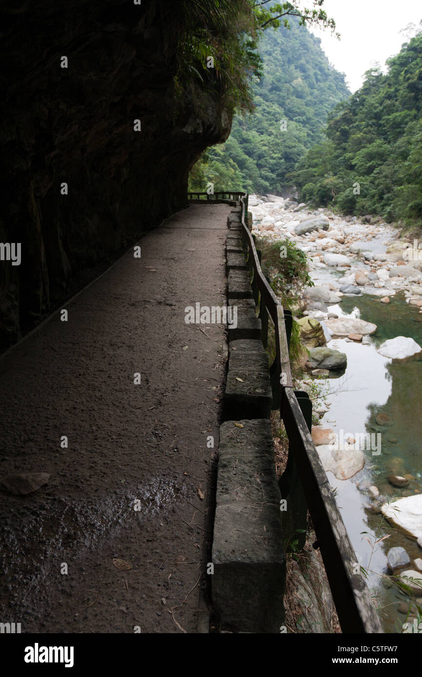 Cliffside trail under rock overhang and crystal clear stream flowing ...