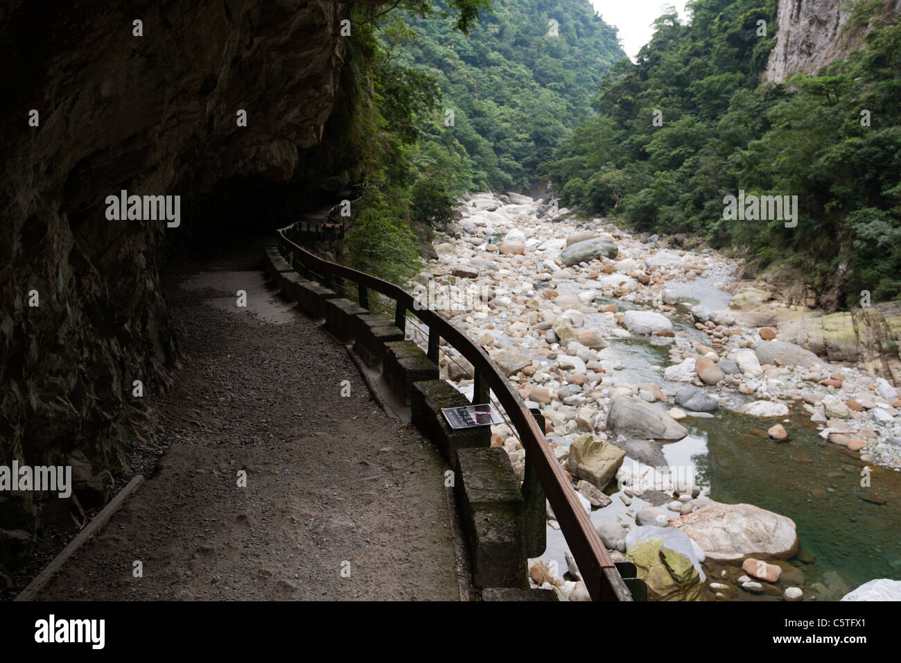 Cliffside trail under rock overhang and crystal clear stream flowing ...