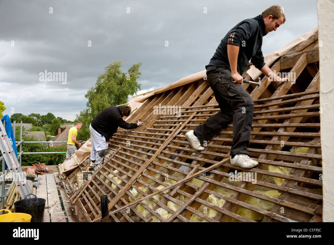 Workmen, having removed the old tiles from part of the roof, now ...