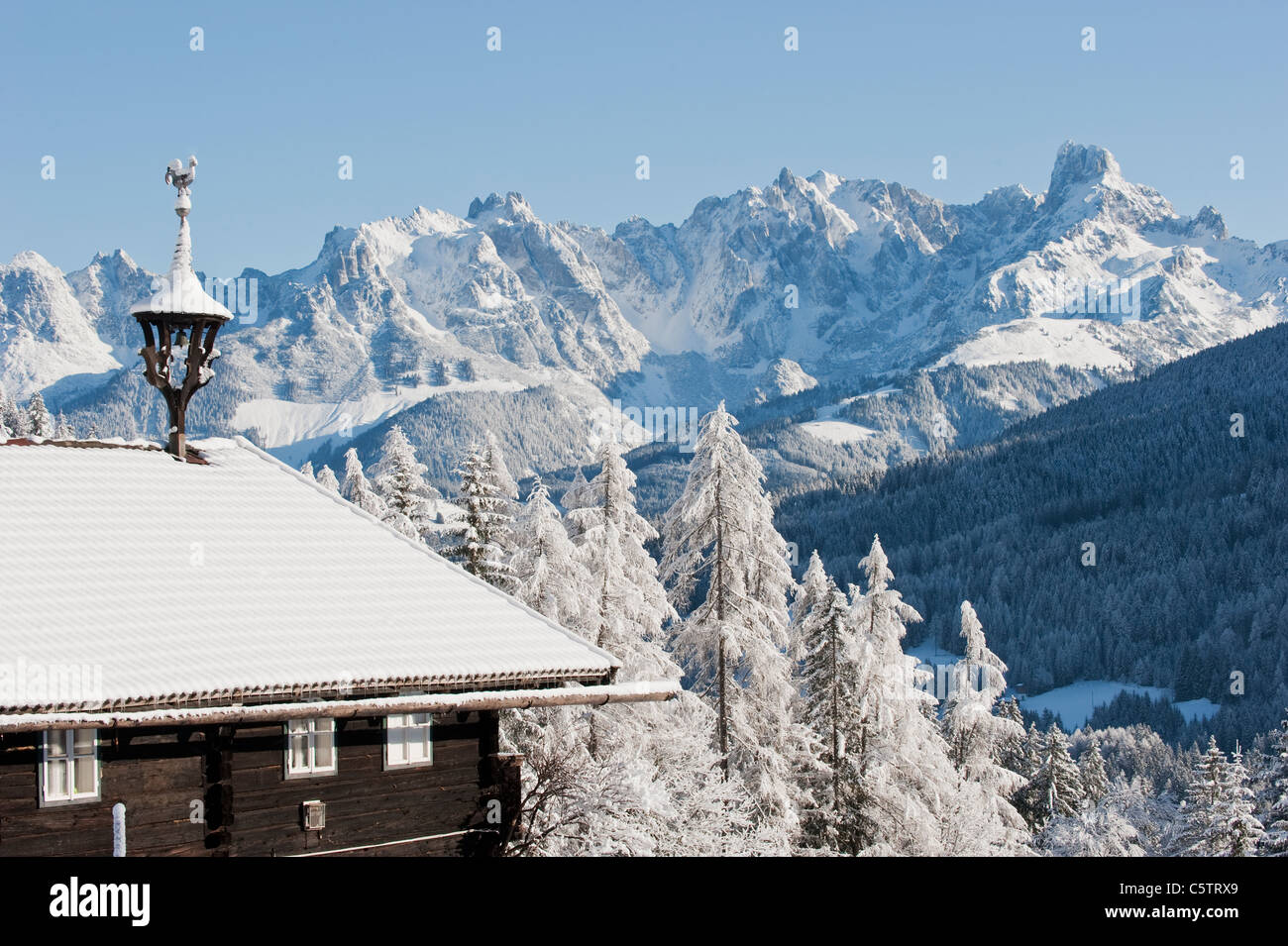 Austria, Salzburg, Snow-covered trees and hut with mountains in ...