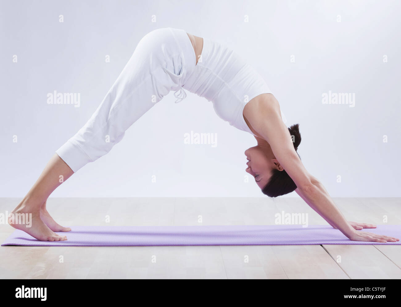 Mid adult woman doing downward facing dog position against white ...