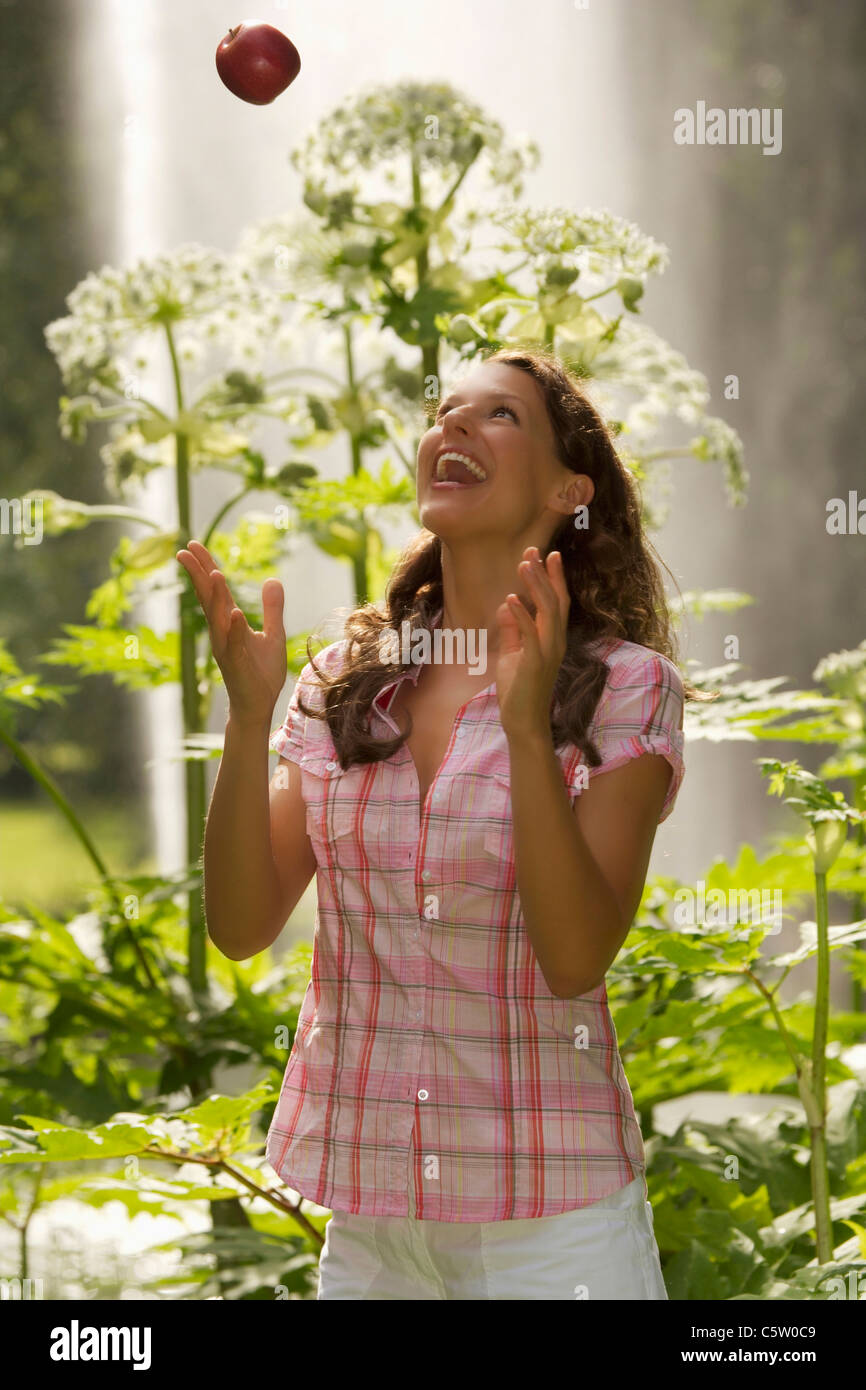 Germany, Bavaria, Young woman throwing apple, laughing, portrait Stock ...